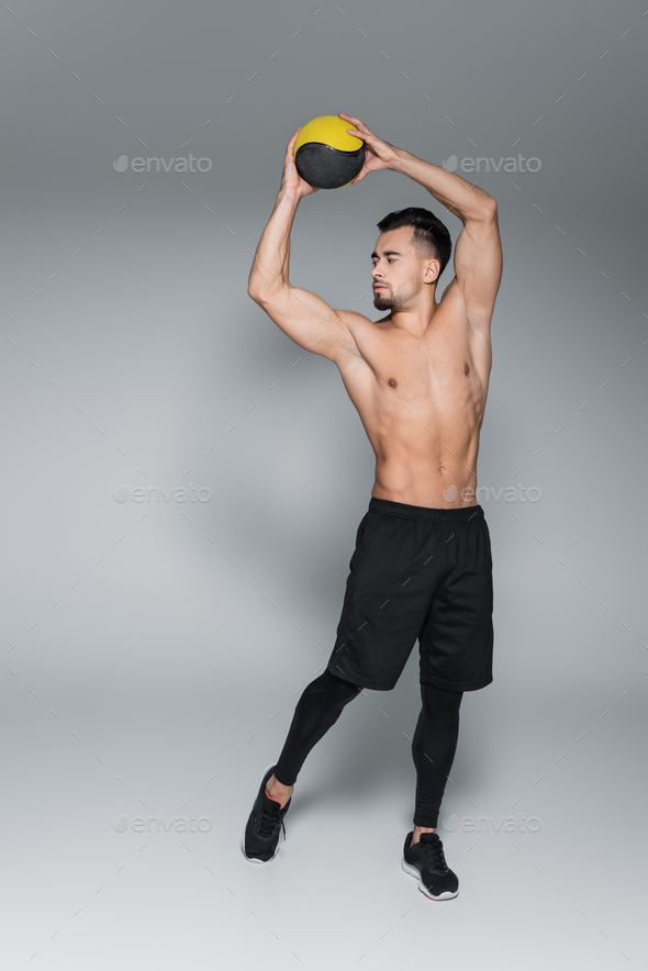 full length of shirtless and bearded sportsman holding ball above head ...