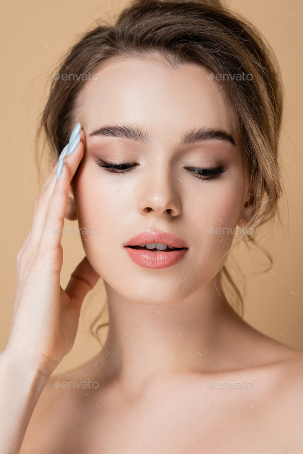 close up view of young and pretty woman touching face isolated on beige ...