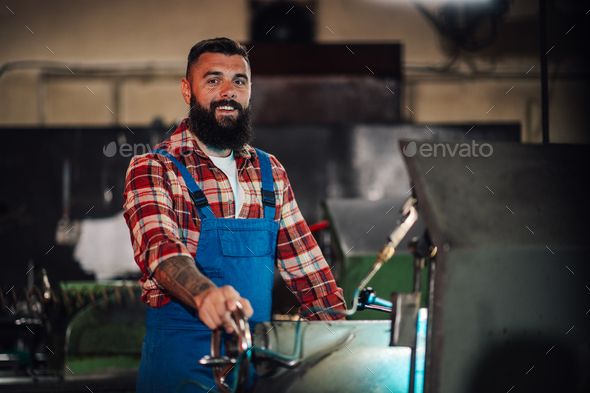 A portrait of a metal turner standing at a lathe machine in a factory ...