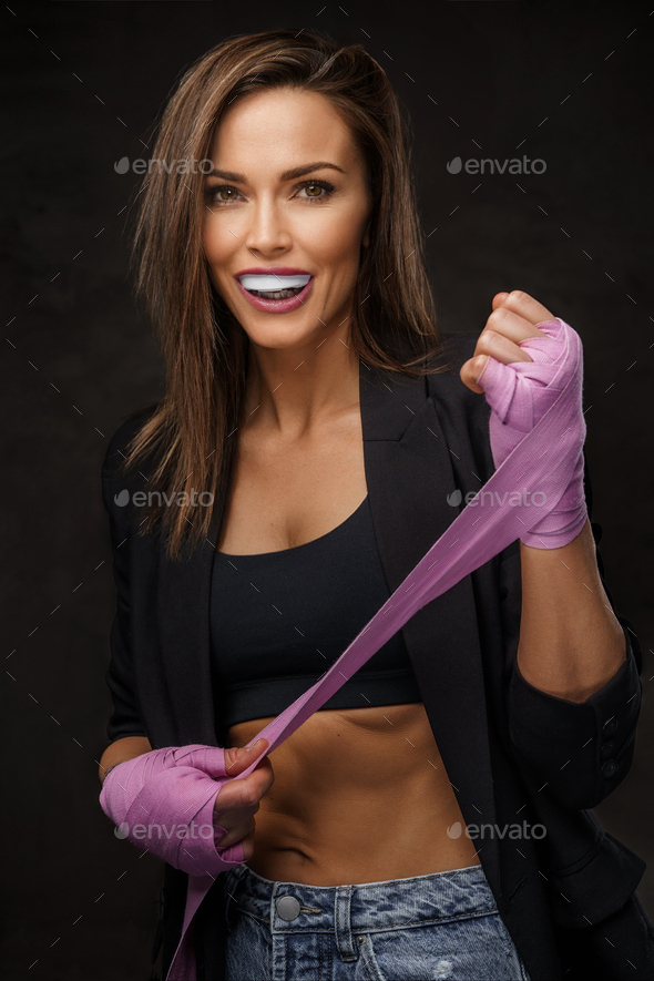 Female boxer with a mouthguard in black attire, winding hand wraps ...