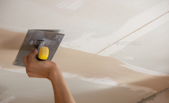 A man puts putty on a plasterboard ceiling. Putty for the joints of ...