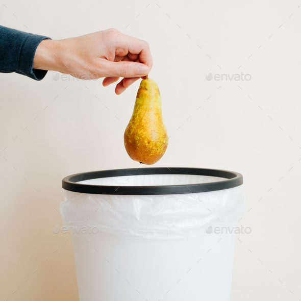 Side view of person hand throwing pear fruit into trash can, close-up ...