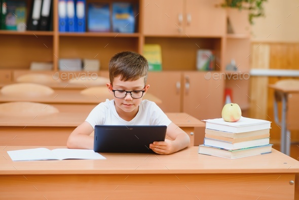 Elementary schoolboy using digital tablet with classmate studying in ...