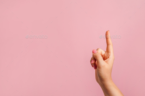 Female hand shows the forefinger up on pink background, copy space ...