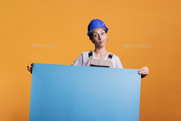 Industrial builder holding blank cardboard sign Stock Photo by DC_Studio