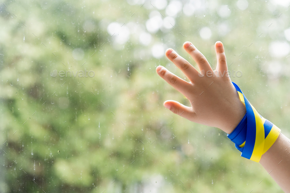 cropped view of child with blue and yellow ribbon touching windows ...