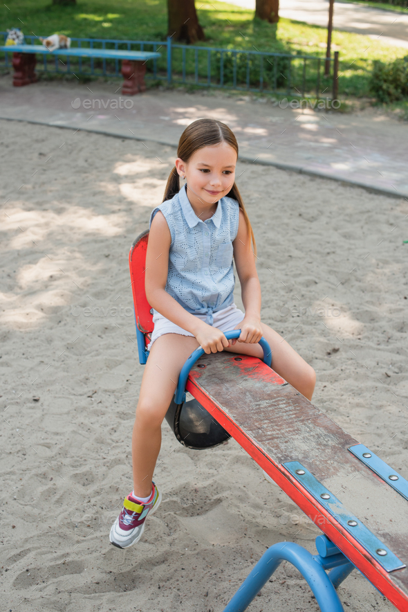 smiling girl in shorts riding seesaw in summer park Stock Photo by ...