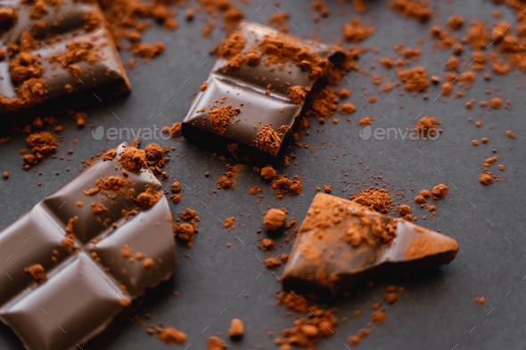 Close up view of dry cocoa powder on chocolate pieces on black ...