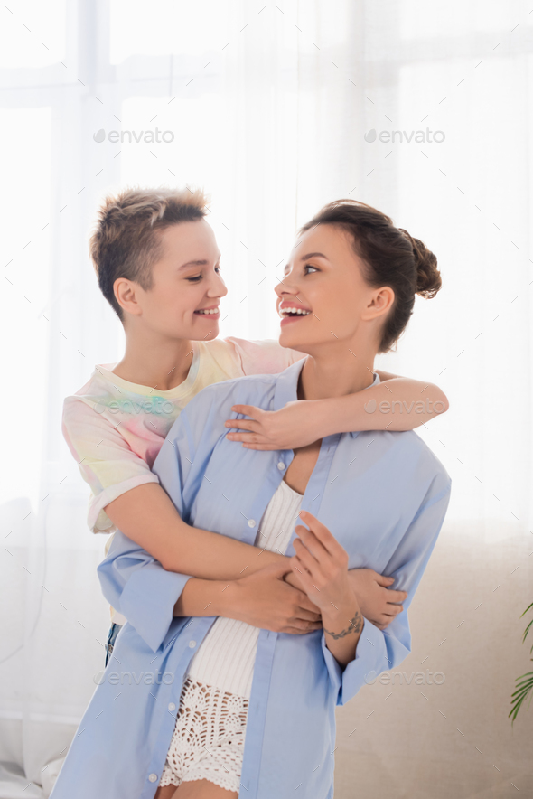 joyful bigender people embracing and smiling at each other at home ...