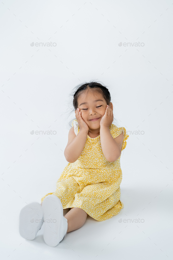 full length of cute asian child in yellow dress smiling with closed ...