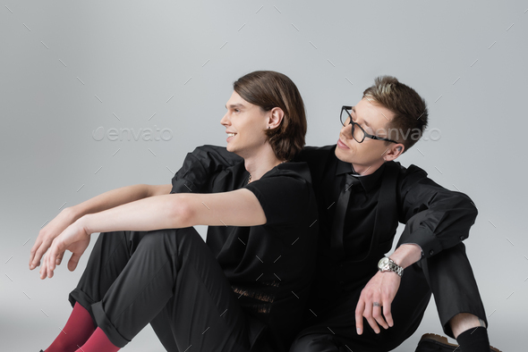 Man in formal wear looking at smiling boyfriend on grey background ...