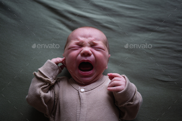 mixed race newborn crying baby lies wrapped in a green muslin swaddle ...