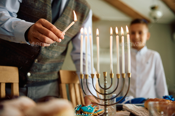 Close up of man lights the menorah while celebrating Hanukkah with son ...