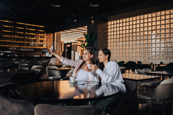 Happy girls posing in a coffee shop while taking selfies. Stock Photo ...