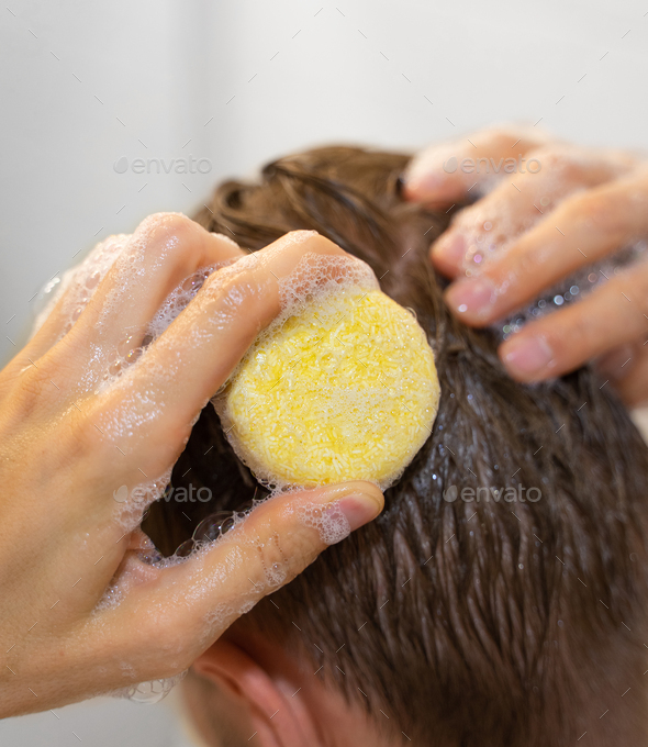 A man uses a solid shampoo bar in the bathroom. An applying shampoo to ...