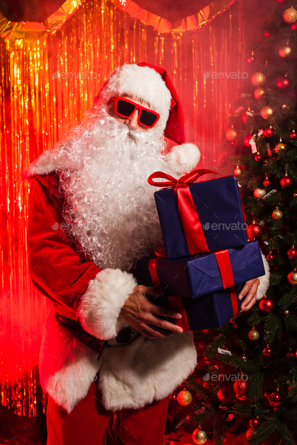 Santa claus in sunglasses holding presents near christmas tree and ...