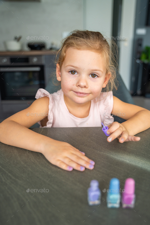 Portrait of little girl doing manicure and painting nails with colorful ...