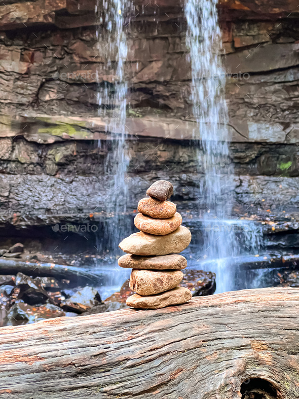Vertical shot of a stack of stones on a log by the waterfall in a ...