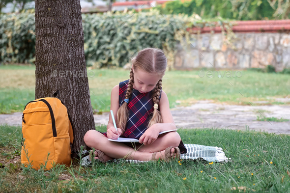 Child young pupil concentrated, studying under a tree in a green city ...