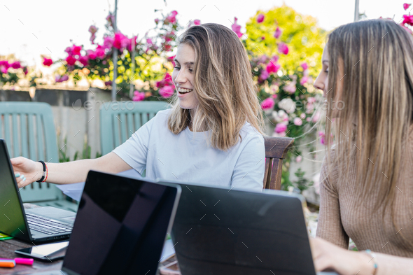 Two smiling girls friends comparing their notes and chatting about what ...