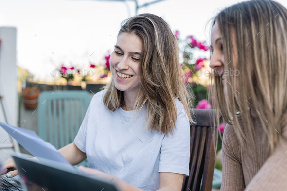 Two smiling girls friends comparing their notes and chatting about what ...