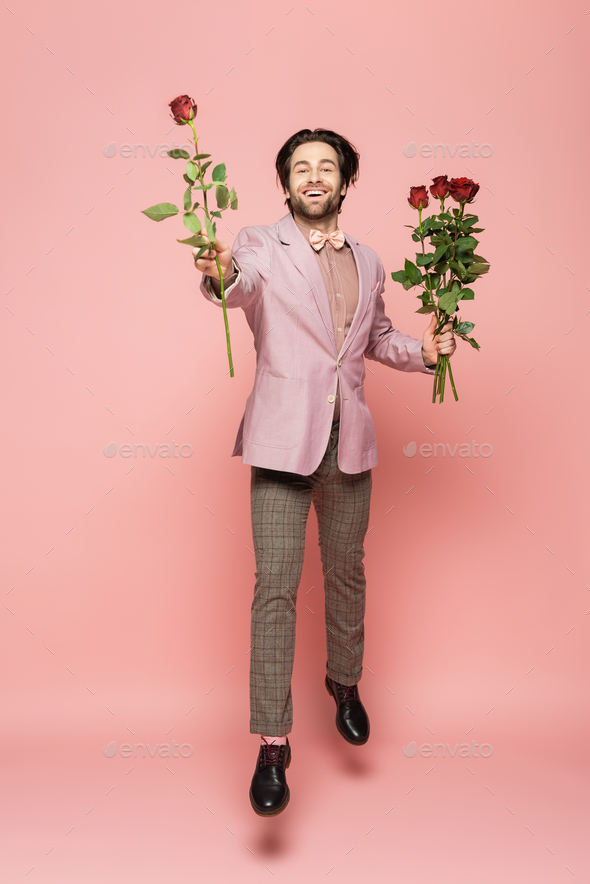 Excited host of event holding roses while jumping on pink background ...
