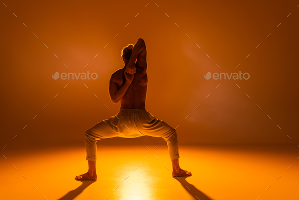 Back View Of Shirtless Man Practicing Goddess Yoga Pose With Clenched