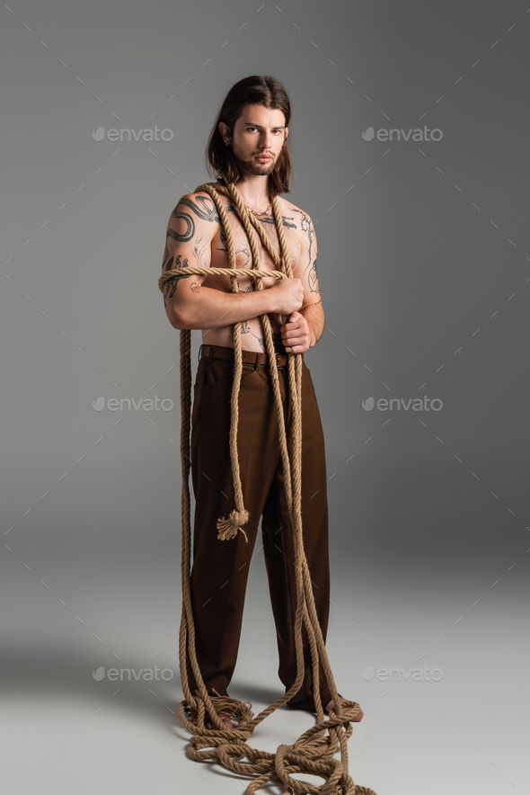 Full length of tattooed man with rope on body on grey background Stock ...
