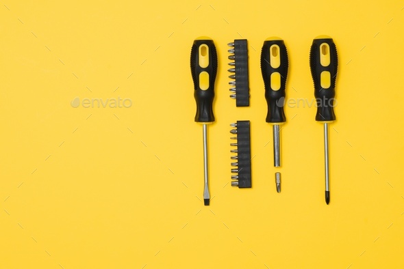 three black and yellow screwdrivers on a yellow background with space ...