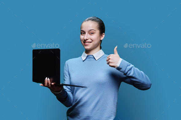 Serious teenage student girl using laptop on blue background, showing ...