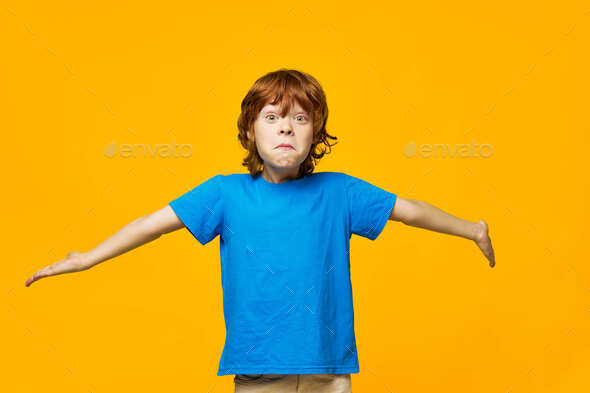 redheaded boy blue t-shirt yellow background freckles shrugs his hands ...