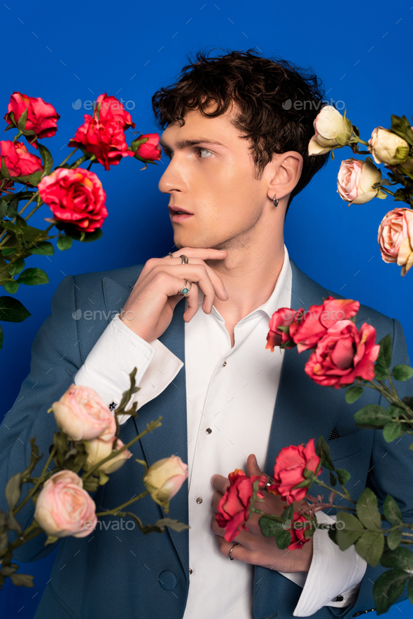 Trendy curly model posing near white and red roses on blue background ...