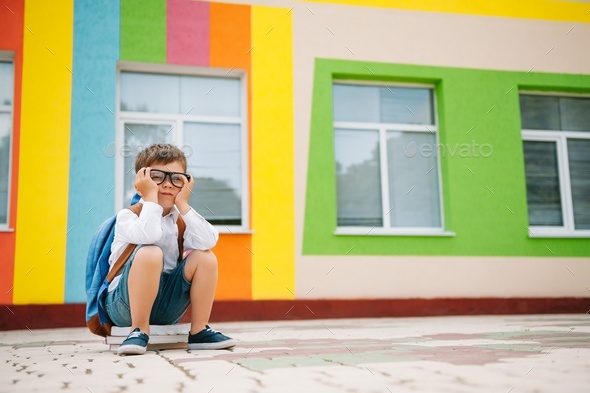 Sad little boy outside of school. Sad schoolboy with books near a ...