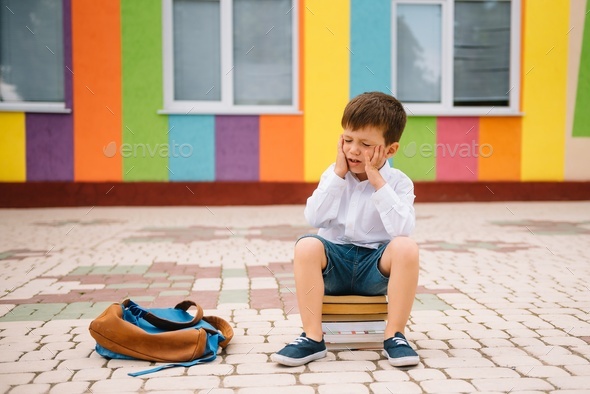Sad little boy outside of school. Sad schoolboy with books near a ...