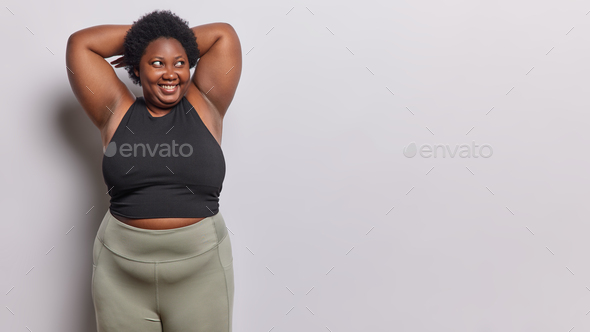 Horizontal shot of positive plus size woman with dark skin keeps arms ...