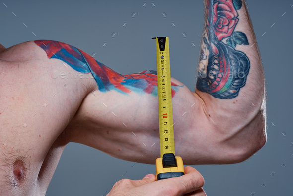 guy measures arm muscles with centimeters on a gray background and a ...