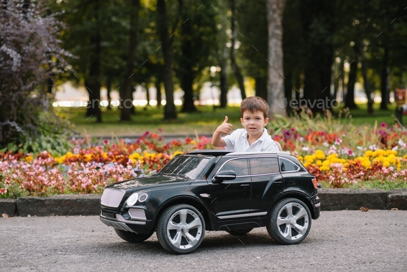 Cute boy in riding a black electric car in the park. Funny boy rides on ...