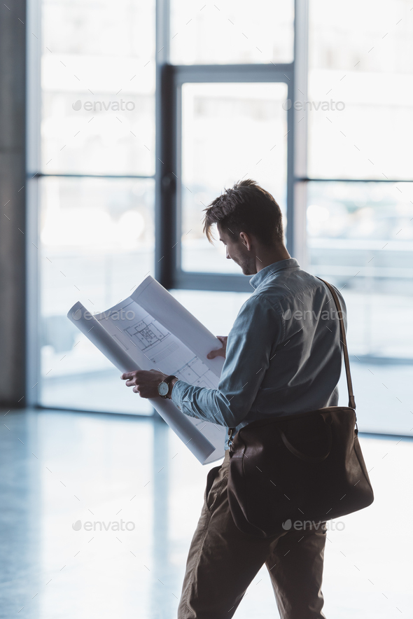 side view of architect looking at blueprint in hands in empty building ...