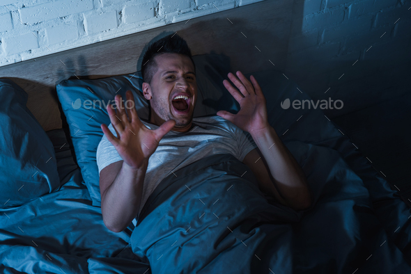 top view of scared young man with ptsd having nightmares and screaming ...