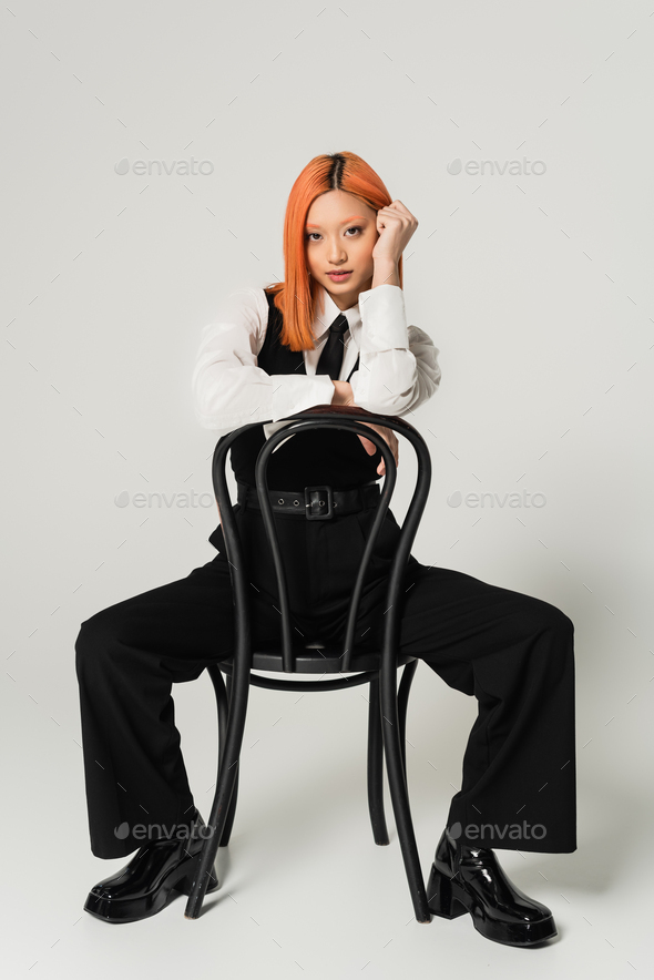 full length of appealing and young asian fashion model sitting on chair ...