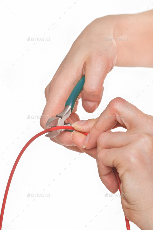 Hand of engineer with metal nippers cutting red electric cable ...