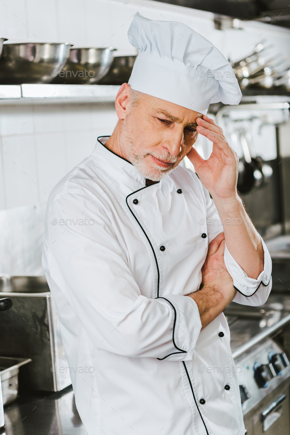 tired male chef in uniform touching head and having headache in ...