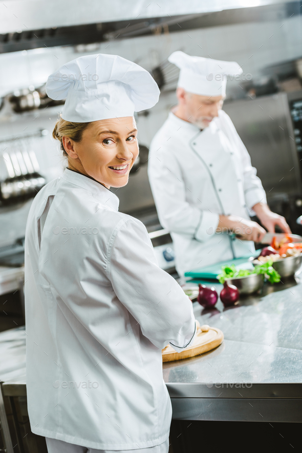 beautiful female chef looking at camera and smiling while cooking with ...