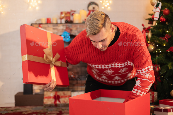 Christmas day concept. handsome man sitting surprised and opening gift ...