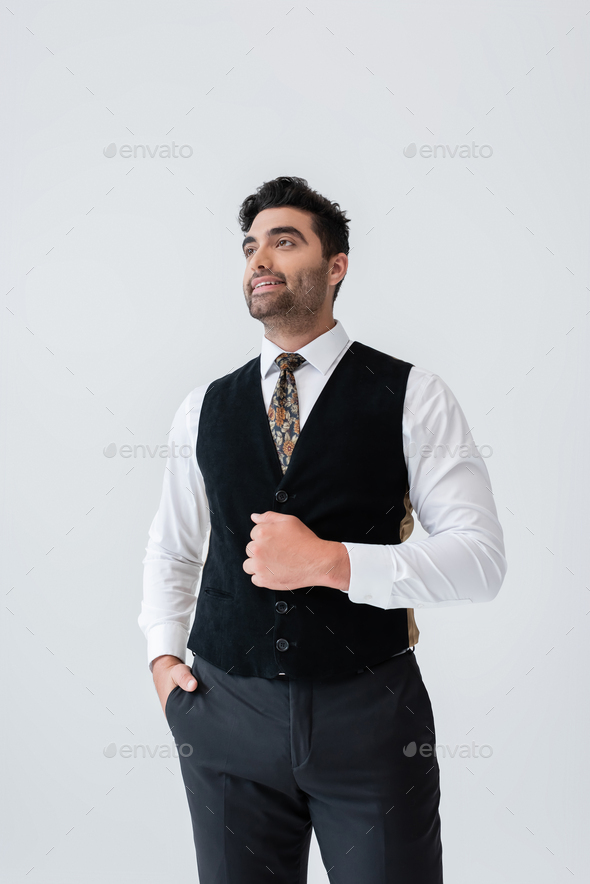 happy muslim man in vest standing with hand in pocket and smiling ...