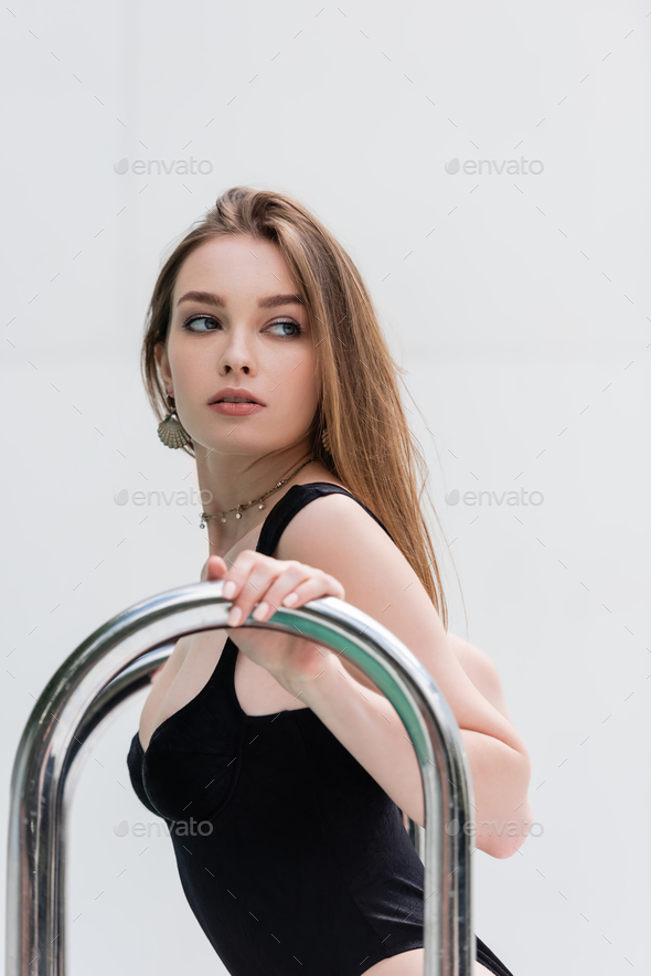 Pretty and stylish woman in black swimsuit touching handrails at resort ...