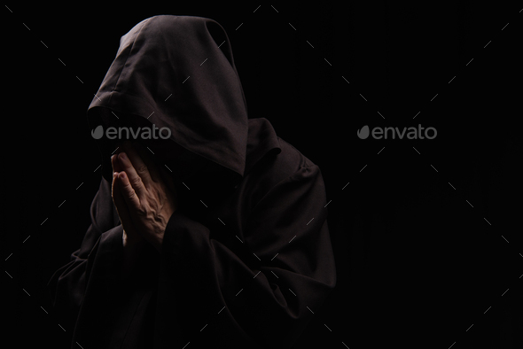 mysterious priest in hooded robe praying isolated on black Stock Photo ...