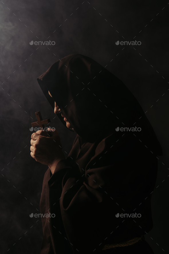 mysterious medieval monk in hooded robe praying with crucifix on black ...