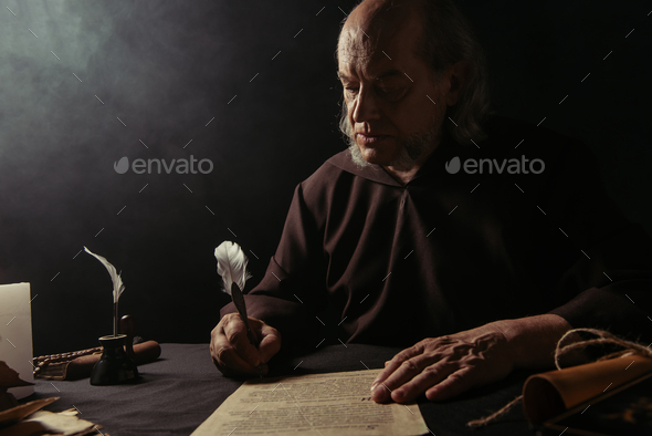 medieval priest in black robe writing manuscript on dark background ...