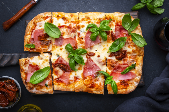Rectangular hot pizza with ham, cheese, dried tomatoes, spicy sauce and ...